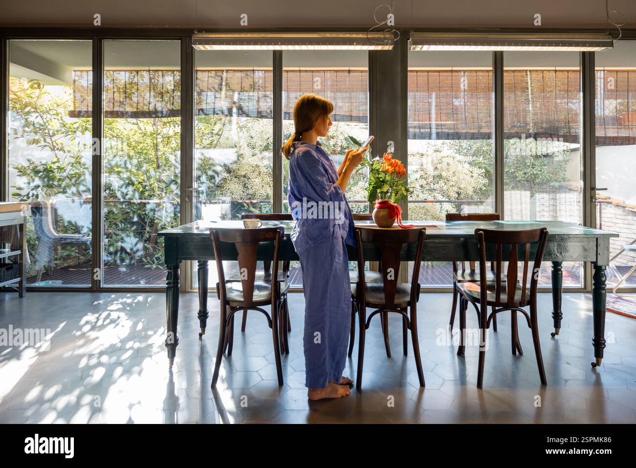 A barefoot woman in a relaxed blue outfit stands by a rustic dining ...