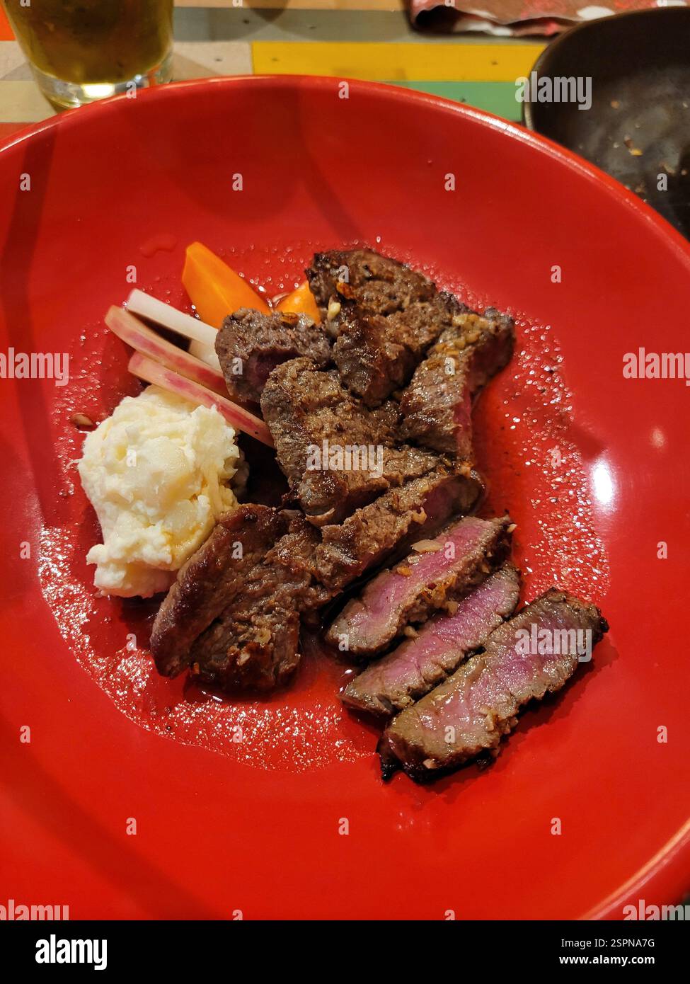 A red plate with steak and mashed potatoes sits on a table Stock Photo ...