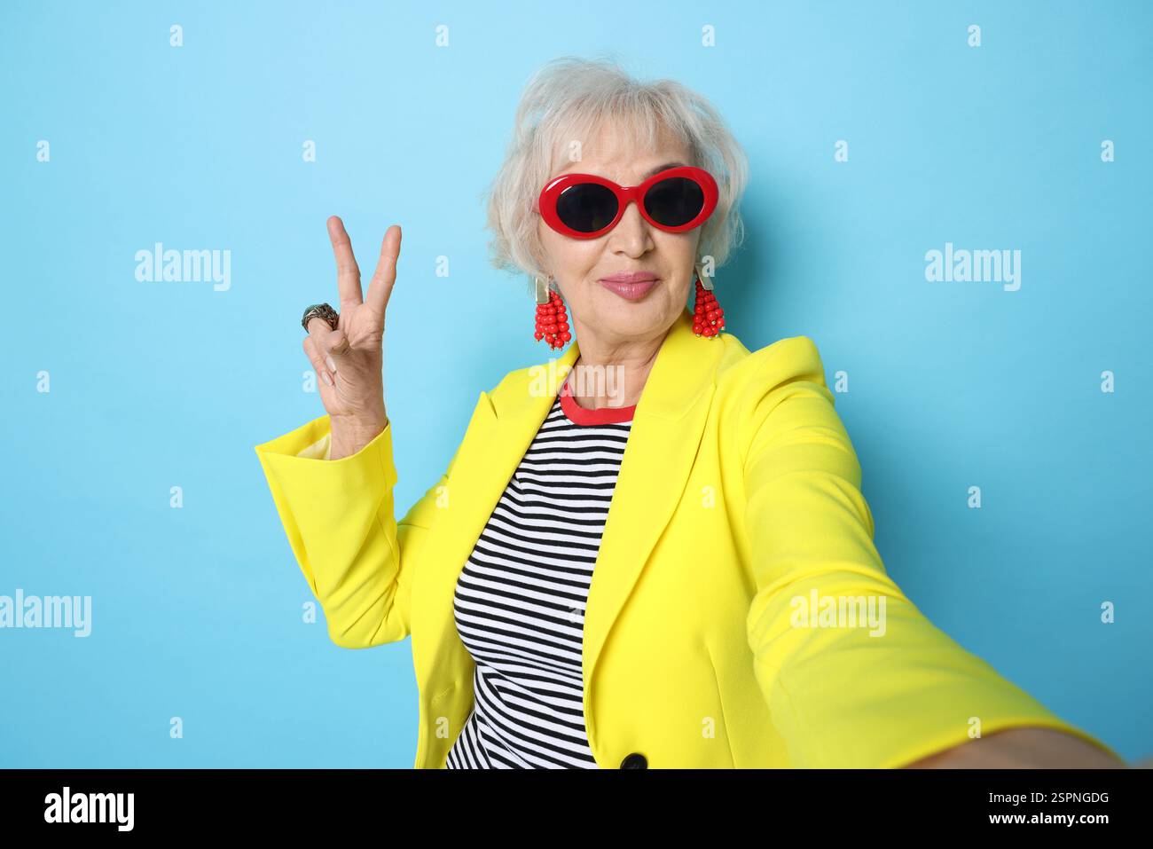 Cool grandmother showing V-sign while taking selfie on light blue ...