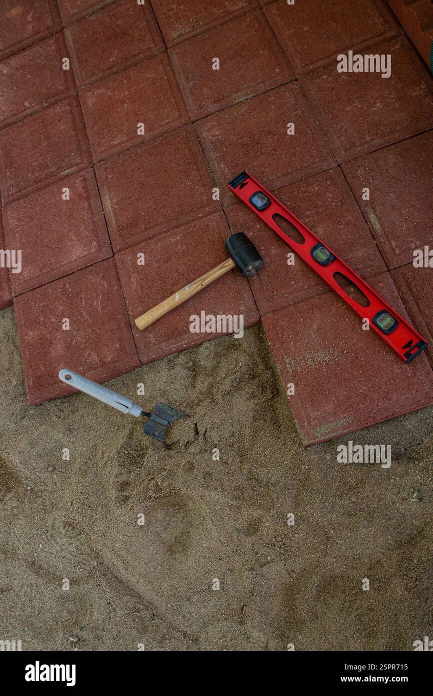 Using a trowel, rubber mallet and a level to build a walkway with red ...