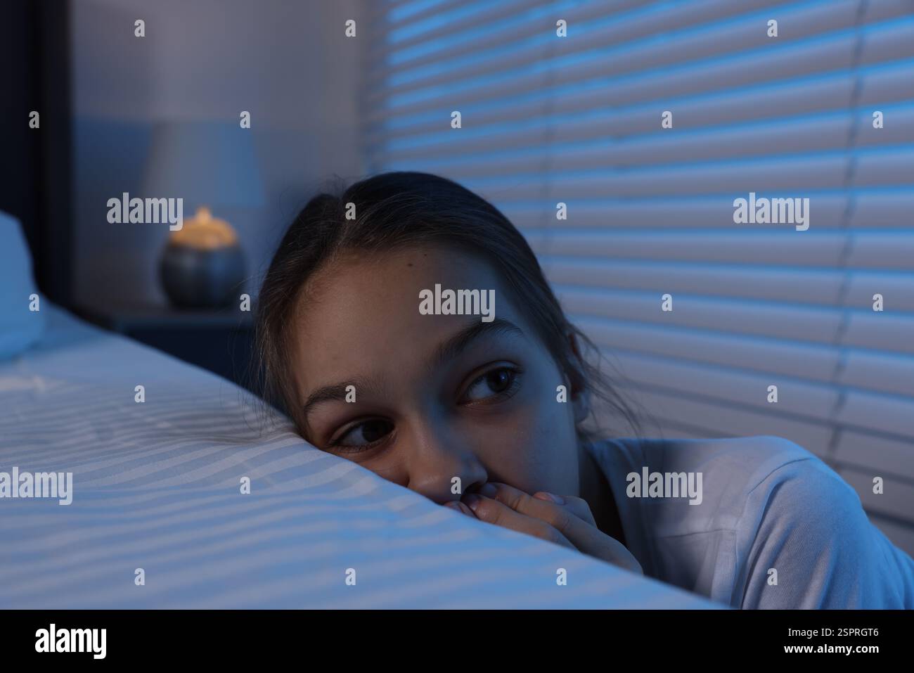 Scared girl hiding behind bed at night Stock Photo - Alamy