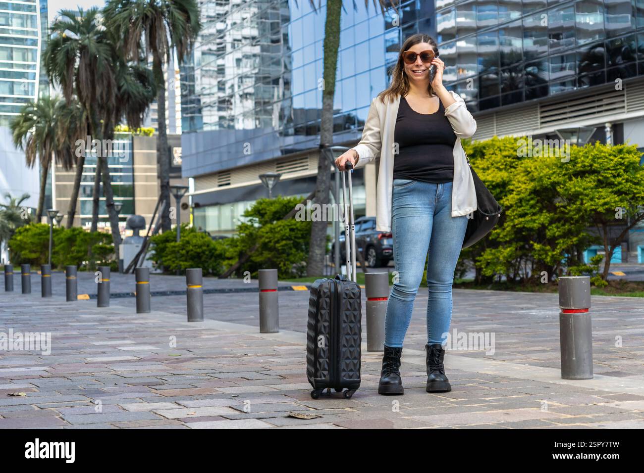 Young businesswoman pulling a suitcase while talking on her smartphone ...