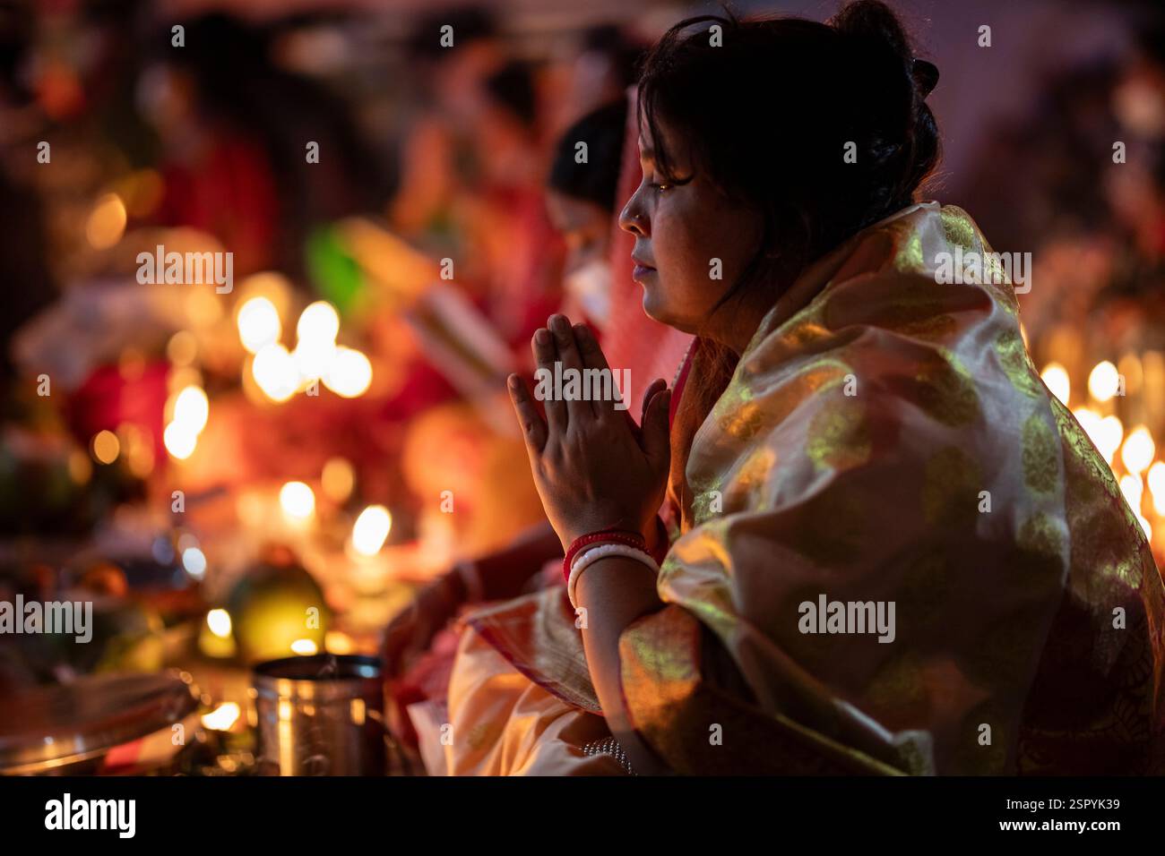 A woman attends in prayer, lighting oil lamps and burning incense as ...