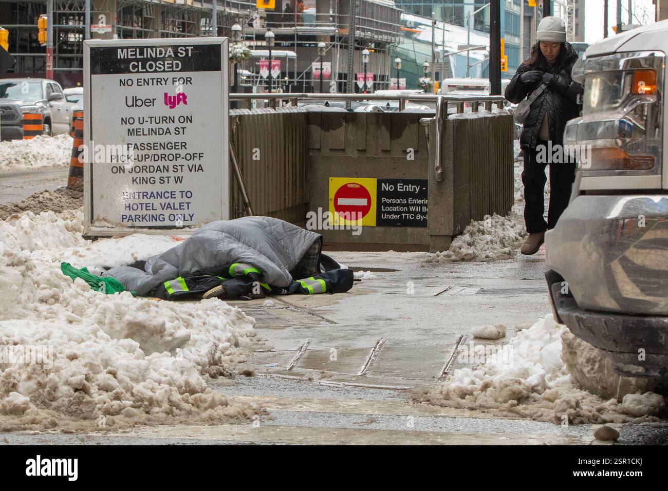 Toronto, Canada, 14th Feb 2025. A homeless man sleeps on a slushy grate ...