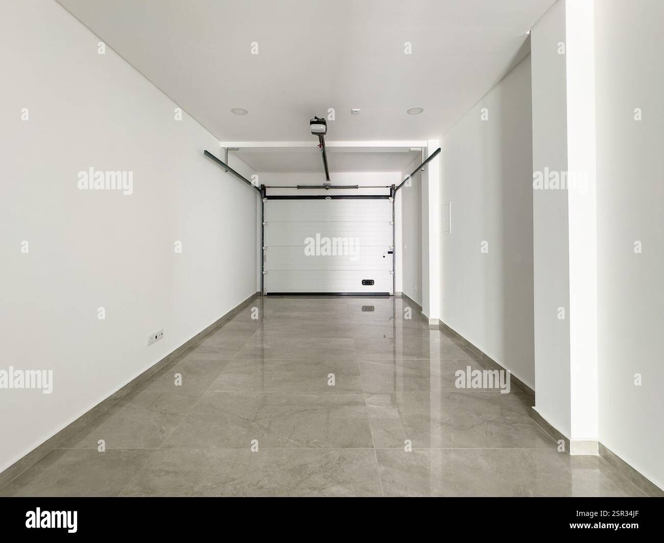 Minimalist garage featuring clean white walls, a motorized door, and ...