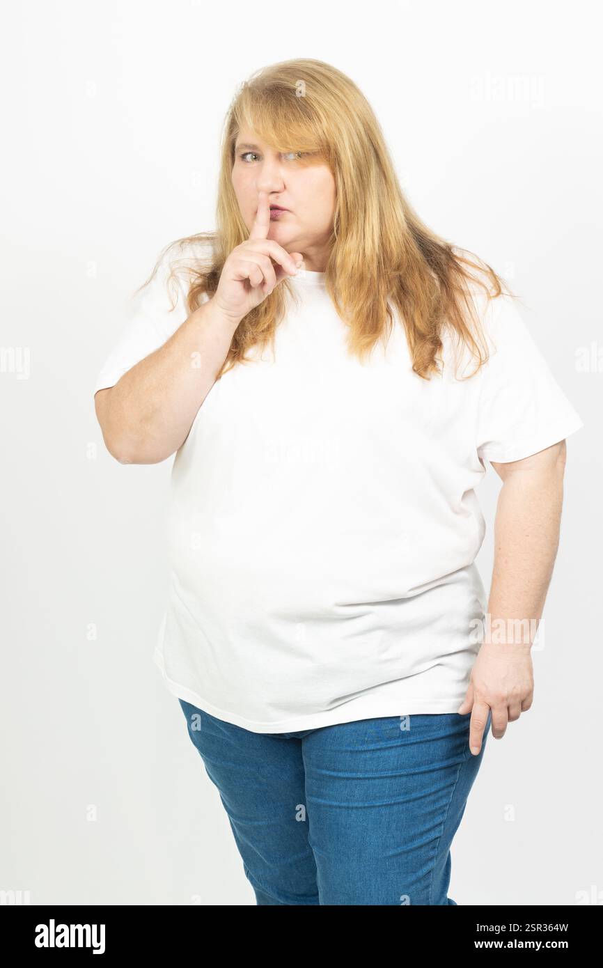 Portrait of a blonde plus size woman with her finger on her lips ...