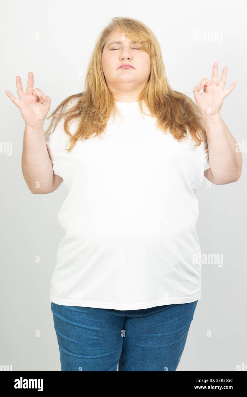 Portrait of a blonde plus size woman with eyes closed, holding an OK ...