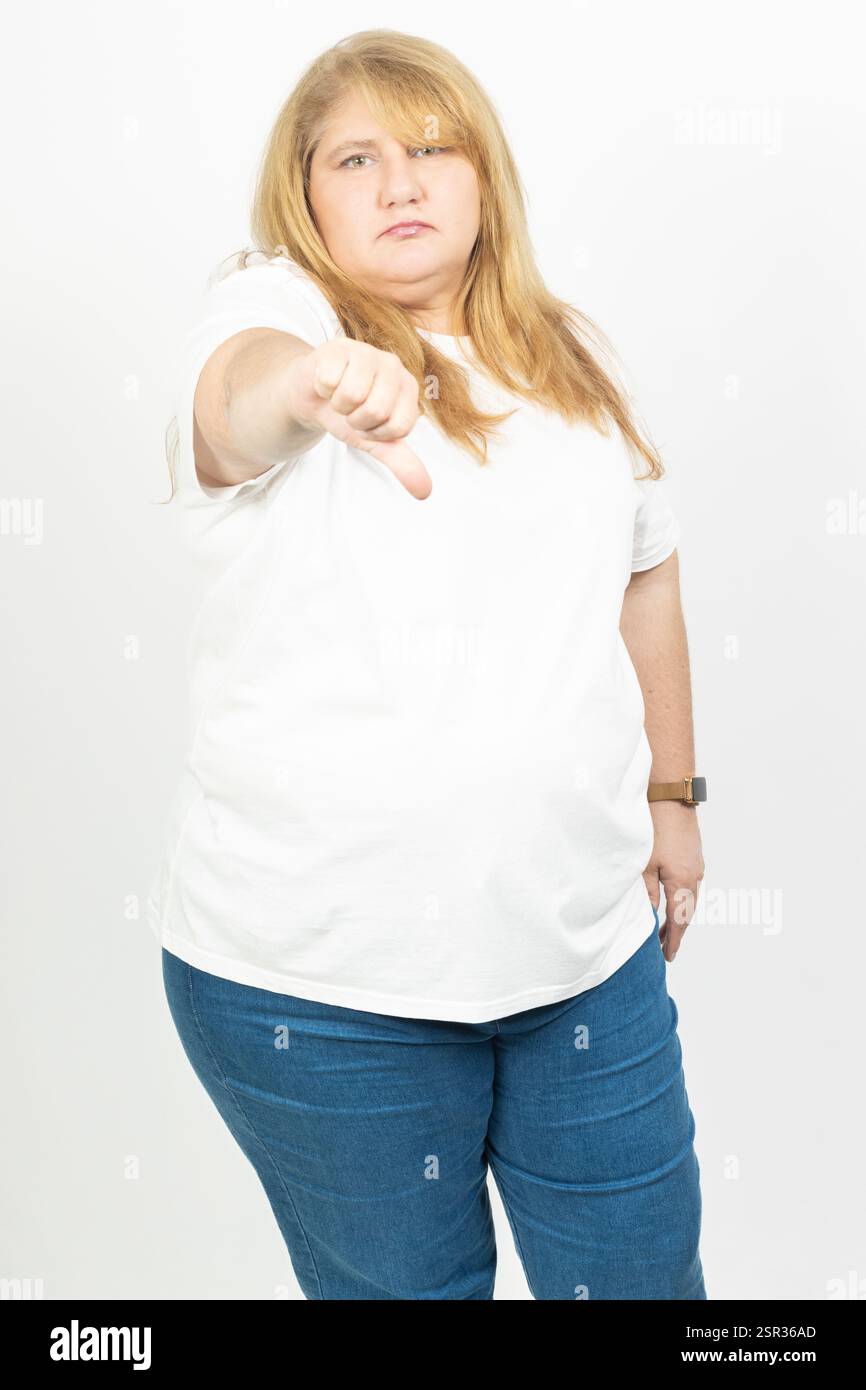 Portrait of a blonde plus size woman giving a thumbs-down gesture with ...