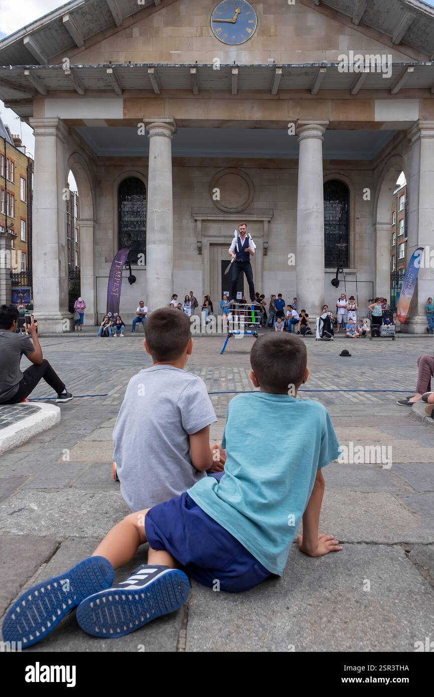 two children watch in rapt attention as an acrobat performs in a street ...