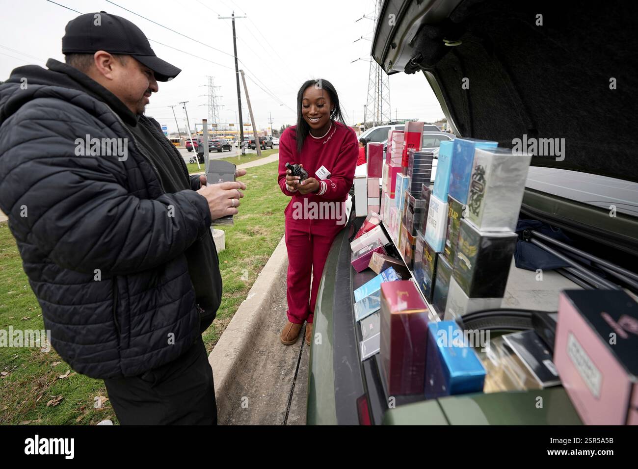 Alex Cacho, left, shows Cali Jones, center, a perfume as he sells Valentine's Day gifts from the ...