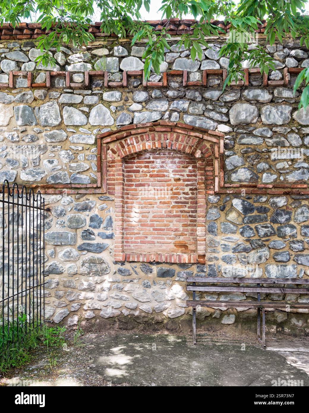 A rustic stone wall features a unique brick archway, surrounded by ...