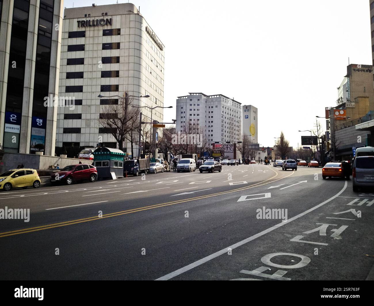 Street scene in South Korea. Cars parked along a wide road. Tall ...