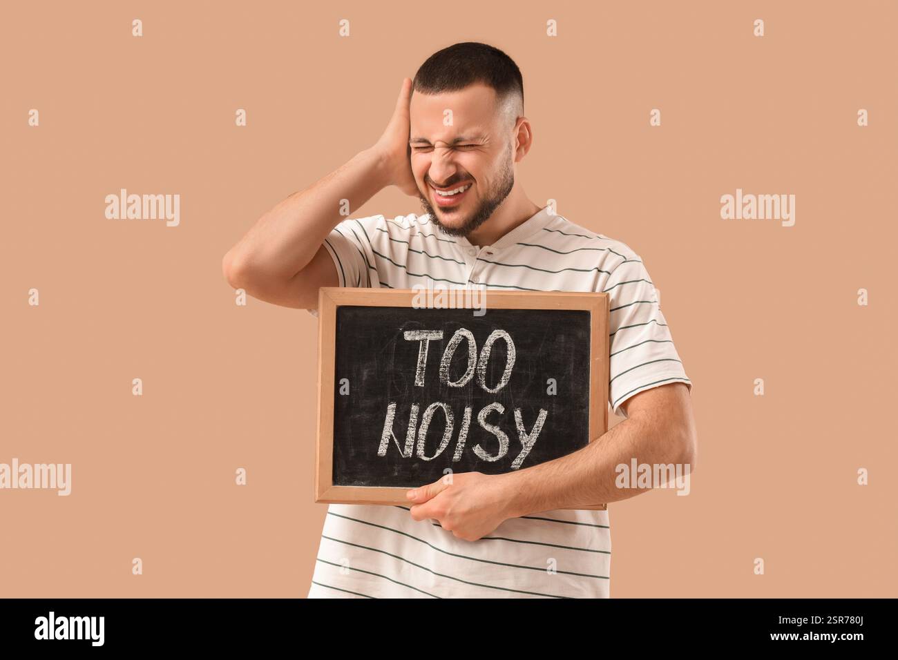 Irritated young man holding chalkboard with text TOO NOISY on beige ...