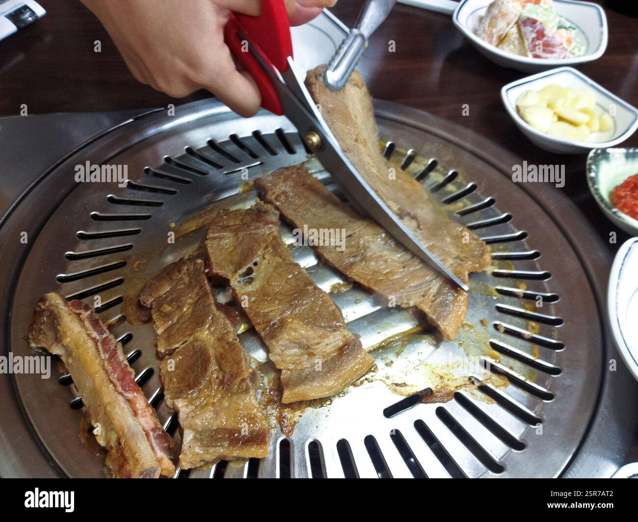 Korean BBQ. Hands using red scissors cut meat on round grill. Steam ...