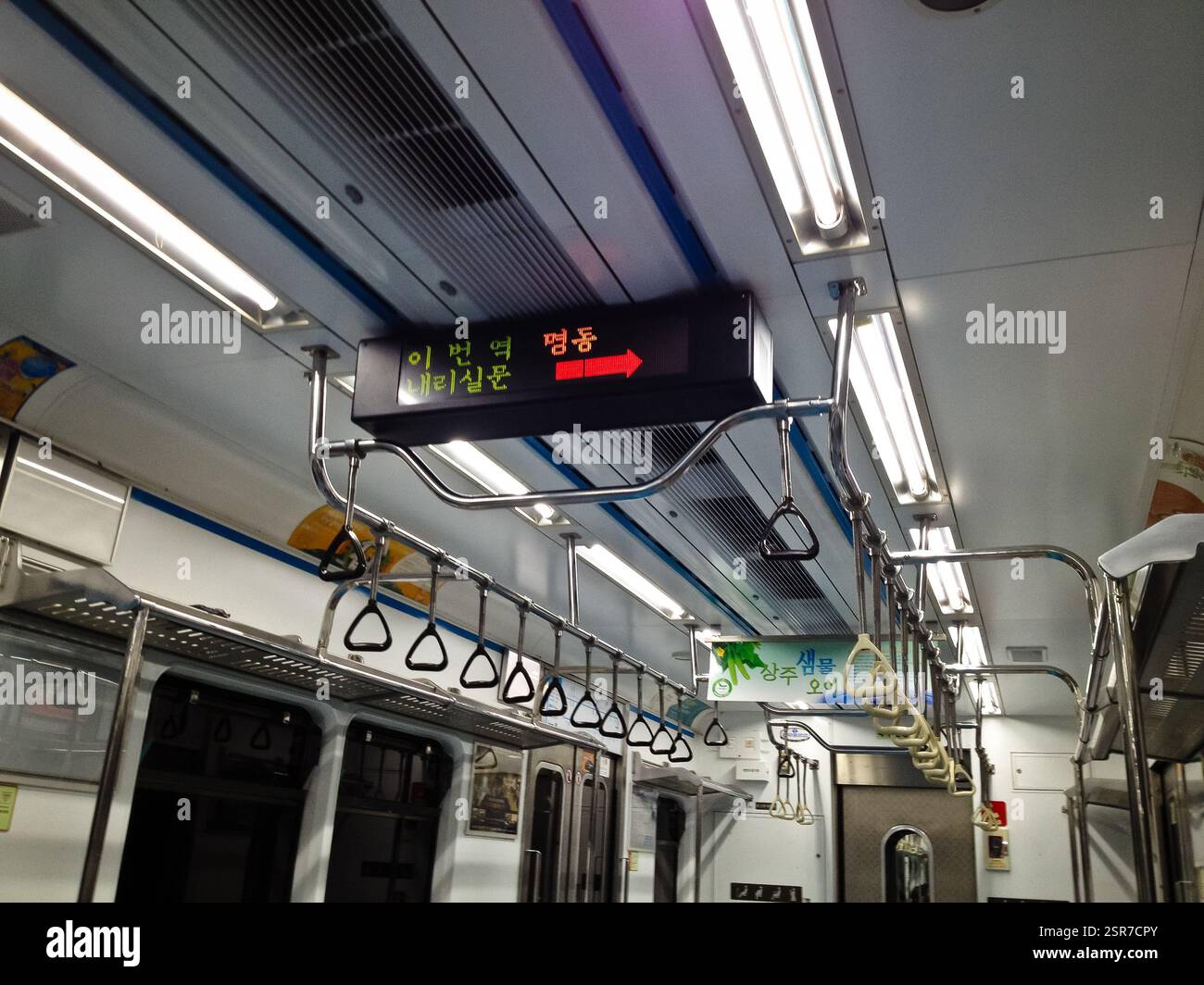 Subway car interior. Red digital sign above handrails. Korean text ...