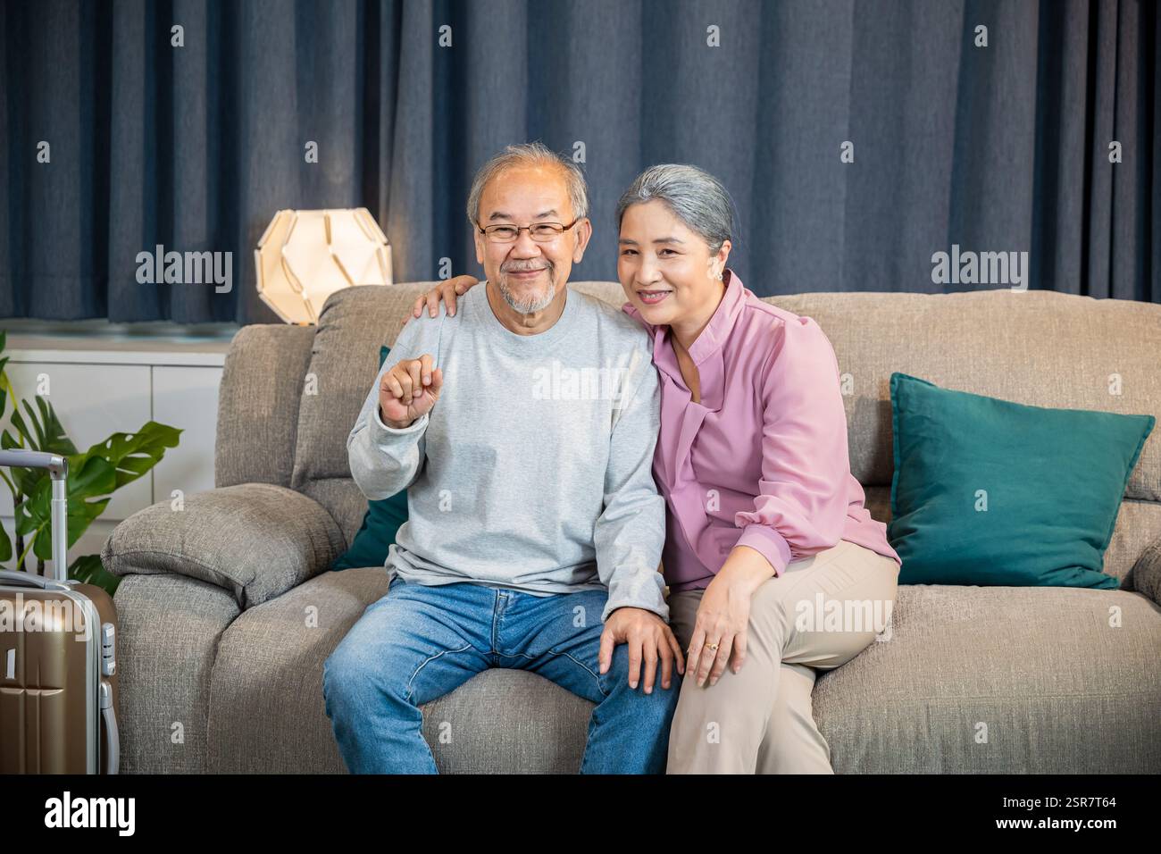 Happy Asian senior couple greeting someone while sitting on a comfortable couch, old man and ...