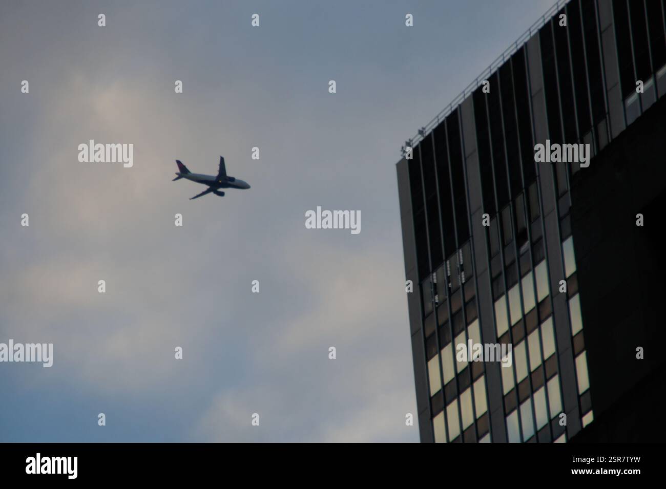 An airplane soars over a black skyscraper in New York City, capturing the dynamic urban ...