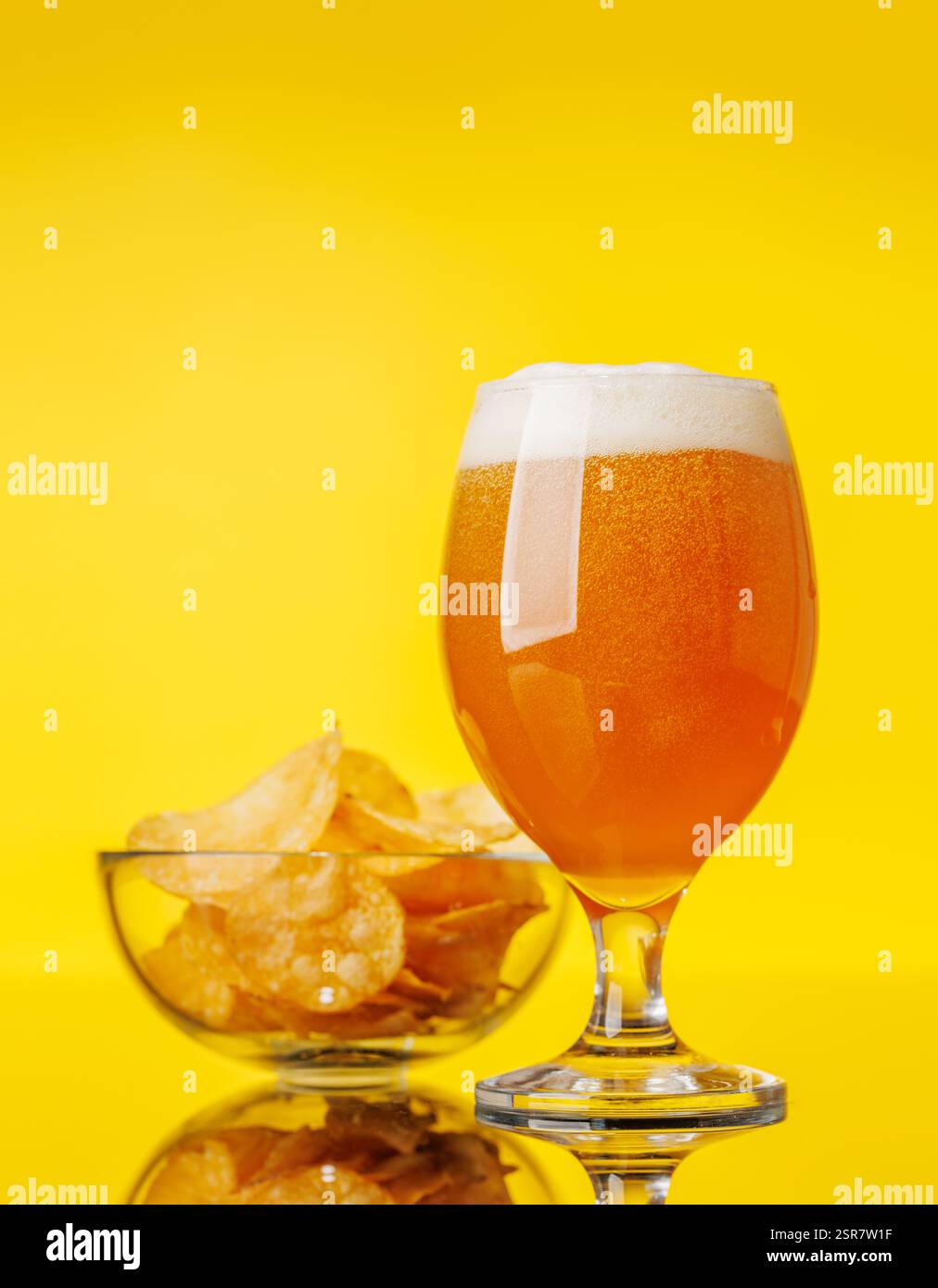 A glass of cold beer alongside a pile of crispy potato chips on a ...