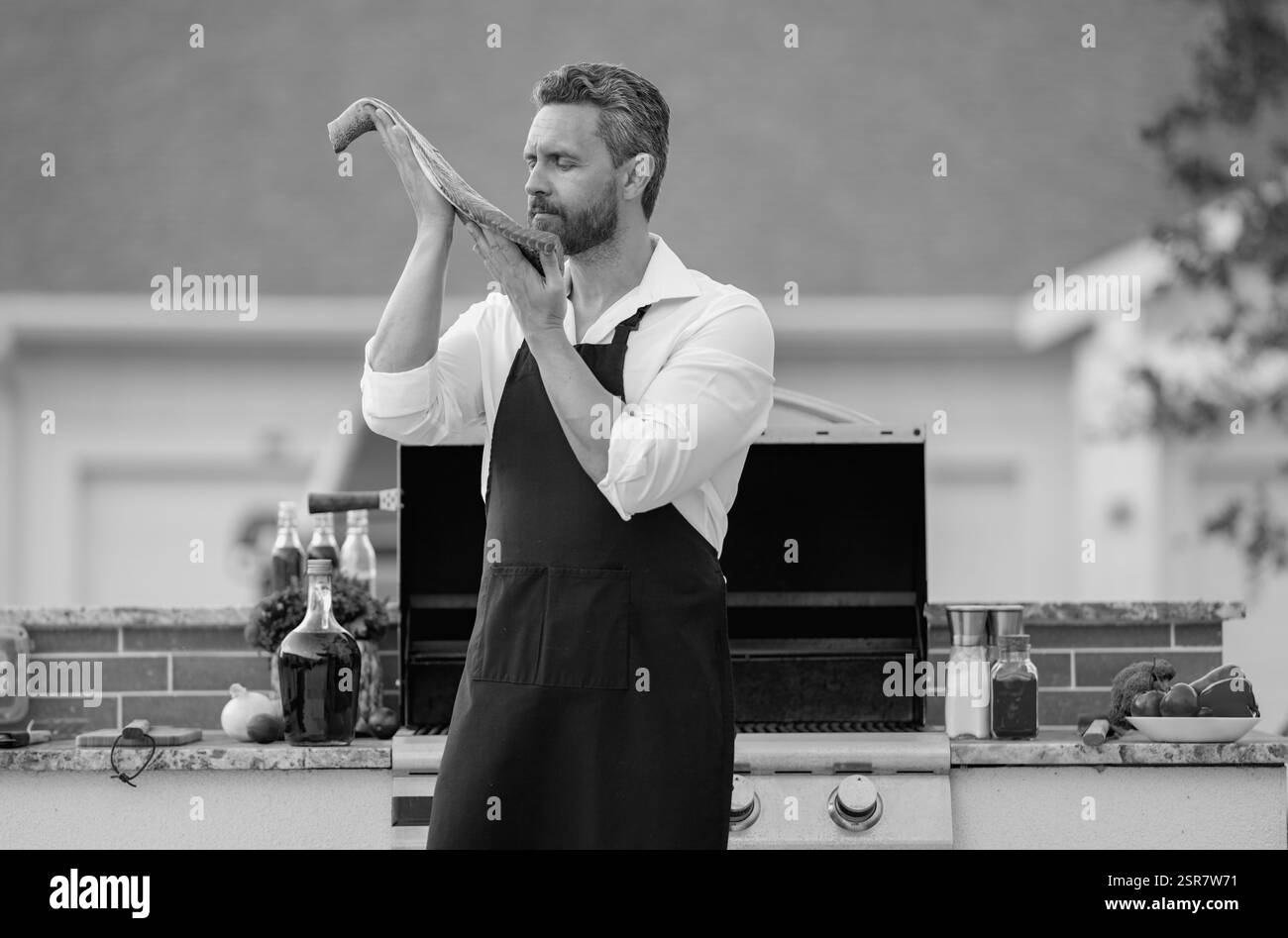 Handsome man in shirt and in cook apron preparing fish on barbecue ...