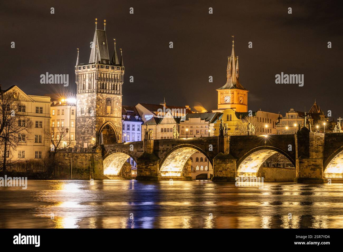 A captivating view of Charles Bridge illuminated at night, reflecting beautifully in the Vltava ...