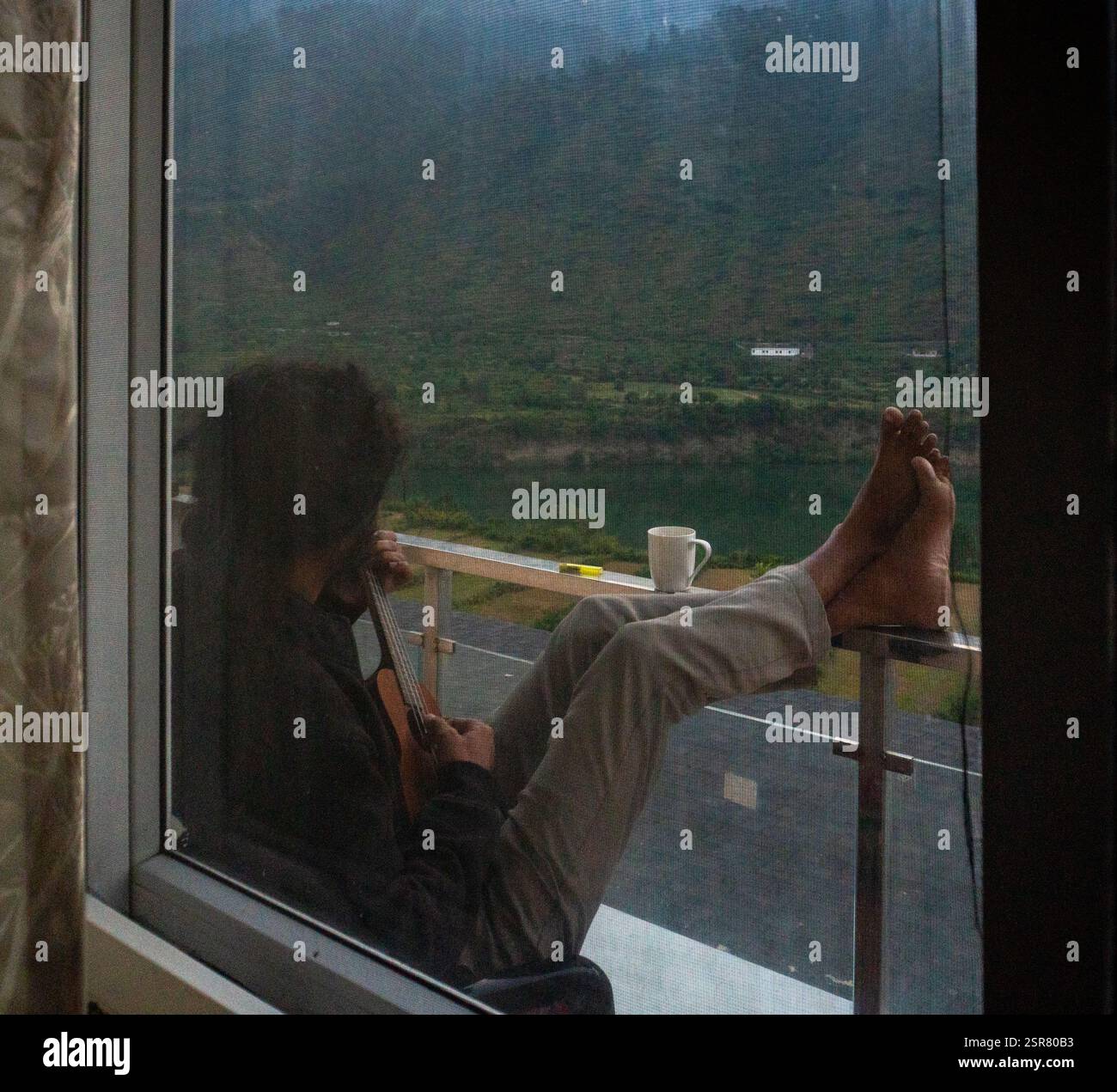 Nov.18th 2024 Uttarakhand India. A serene moment of a man playing ukulele on a hotel balcony ...
