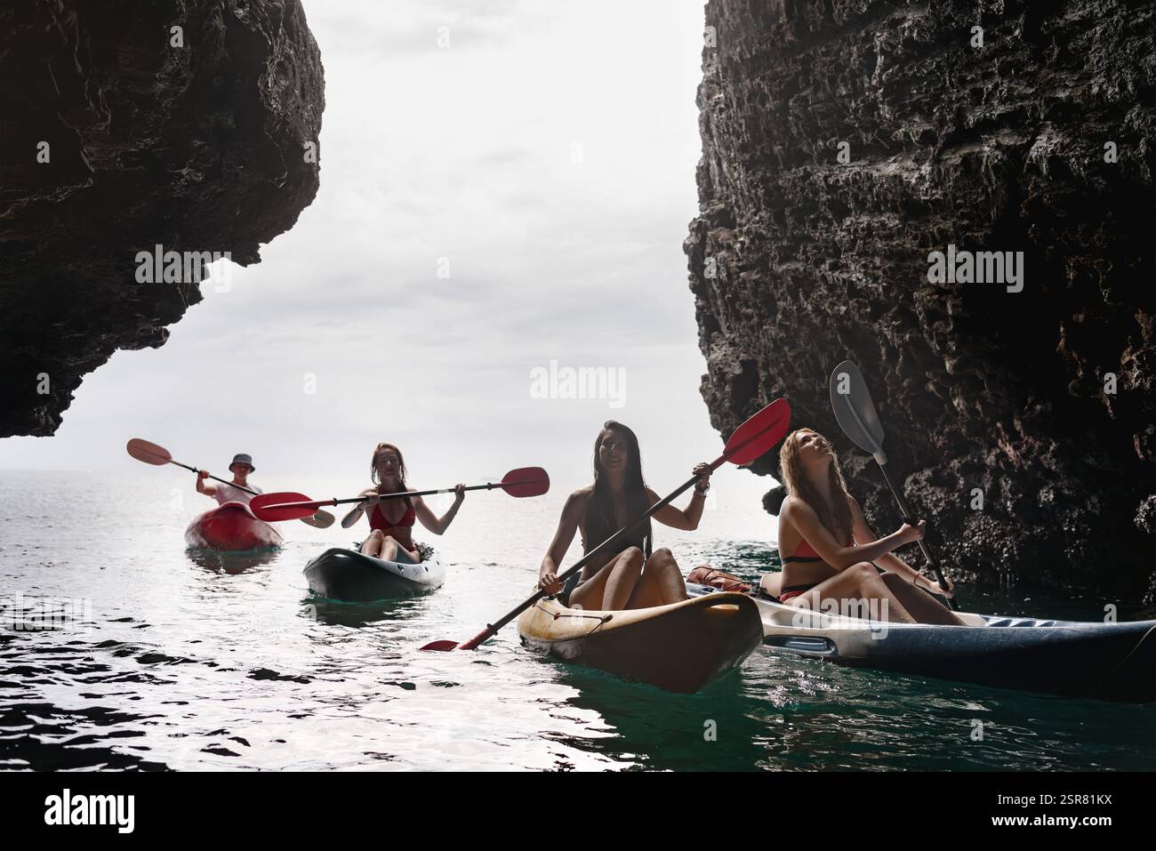 Group of young tourists are floating on kayaks between big sea rocks ...