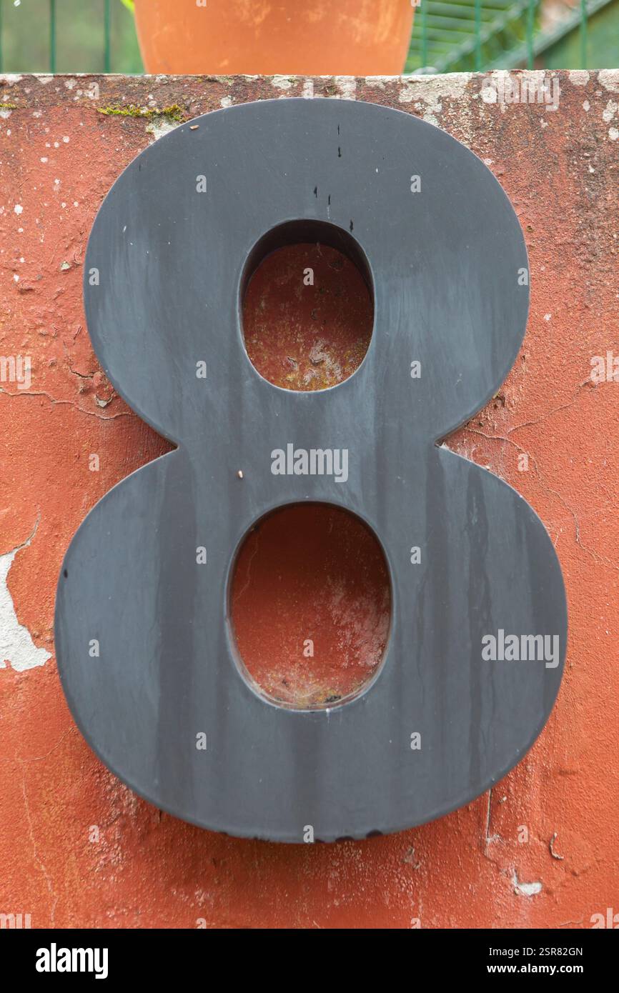 House number 8. Black painted iron over red weathered wall. Houses with ...