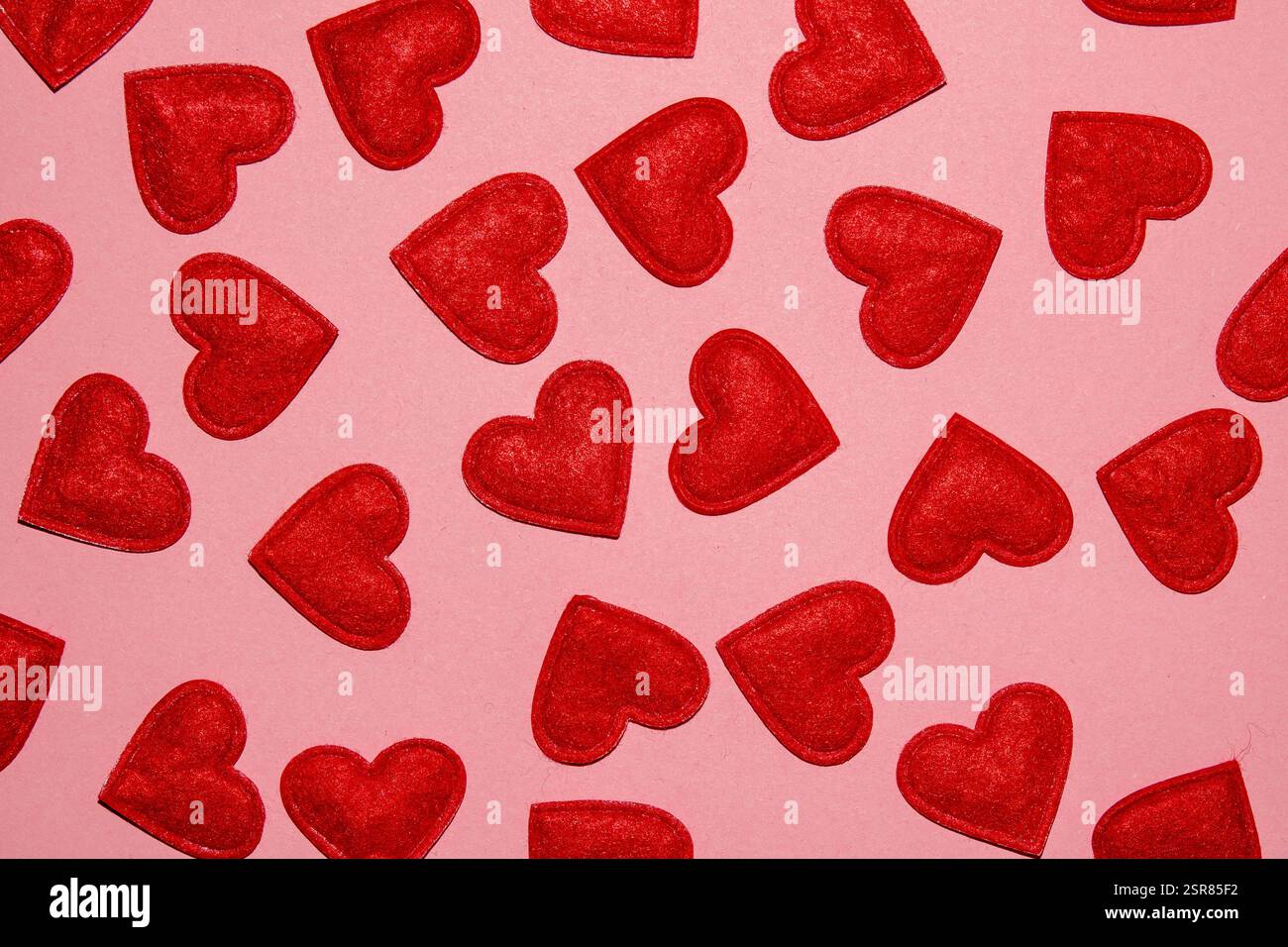 A variety of red hearts are spread across a soft pink background ...