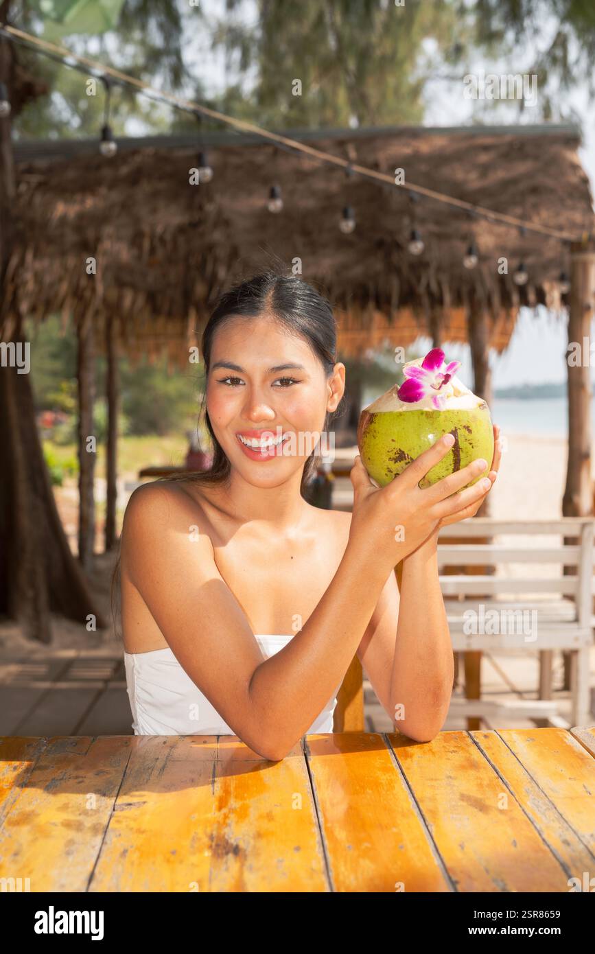 Happy young Asian woman relaxing on the beach holding fresh coconut ...