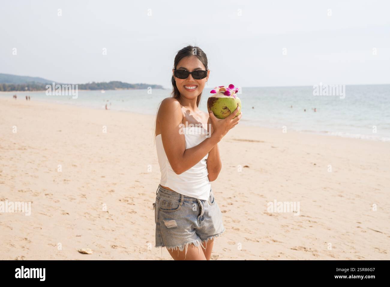 Young beautiful Asian woman smiling with coconut on beach Stock Photo ...