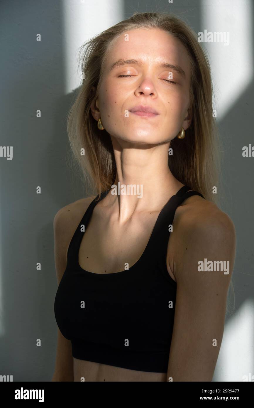 Young serene woman with closed eyes enjoys the warm sunlight on her ...