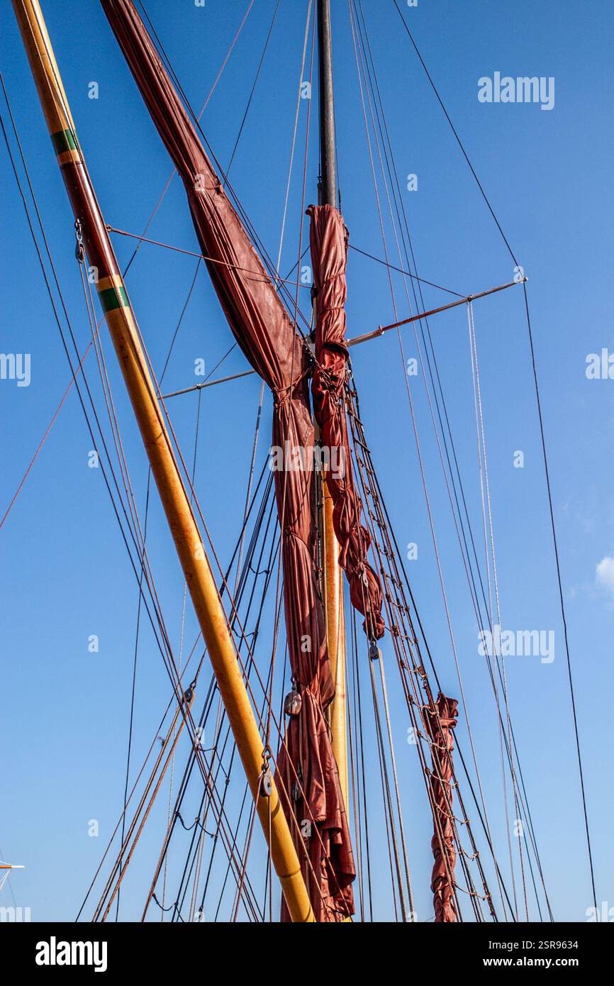 Masts, rigging and furled sails on sailing barge moored on Faversham Creek in sunshine against ...