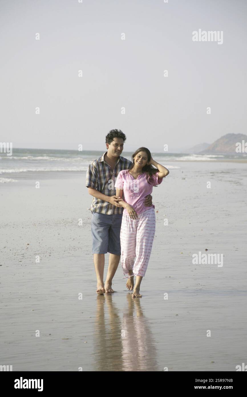 South Asian Indian young man and woman holding hands walking together on seashore, Shiroda, Dist ...