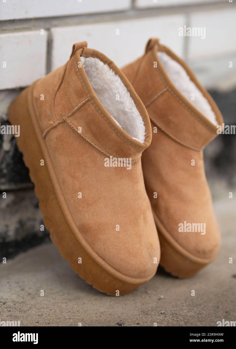 Camel-colored winter boots with fur inside leaning against a white wall ...