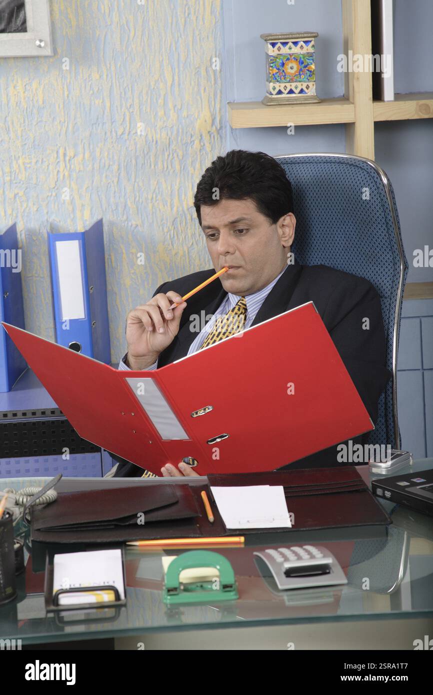 Executive sitting in cabin open red file in hand thinking with holding ...