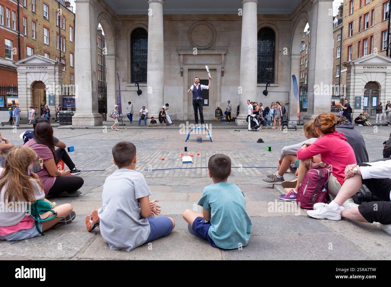 a street performer juggles swords over a platform with the audience ...