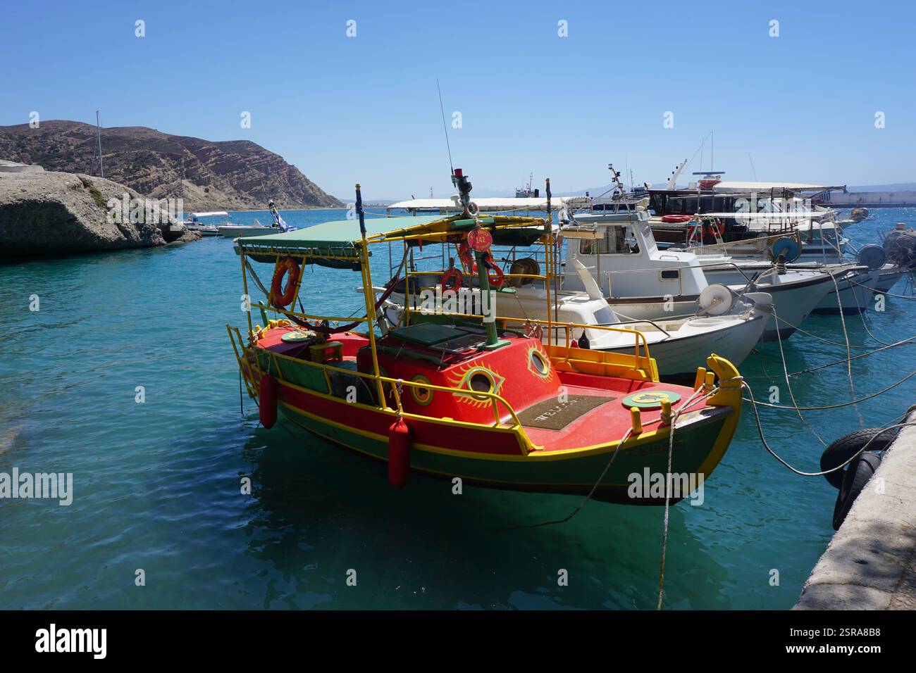 A vibrant fishing boat is secured with other vessels in the port. It ...