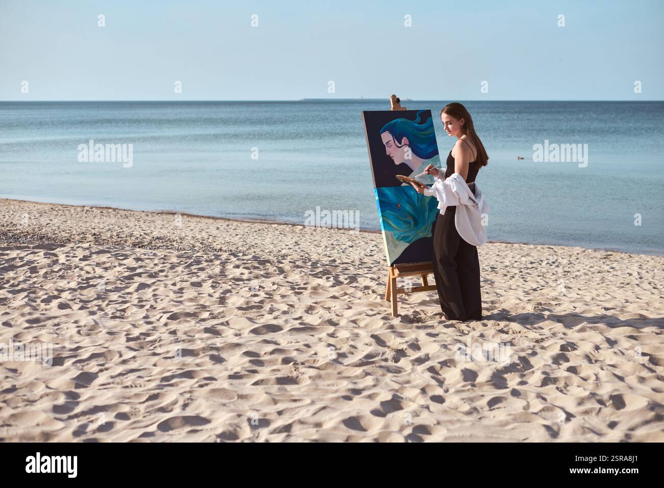 Young woman artist paints vibrant portrait on sandy beach, capturing ...
