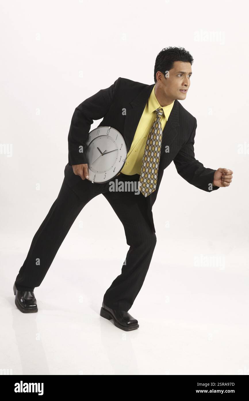 Businessman holding wall clock in one hand next his right side of waist ...
