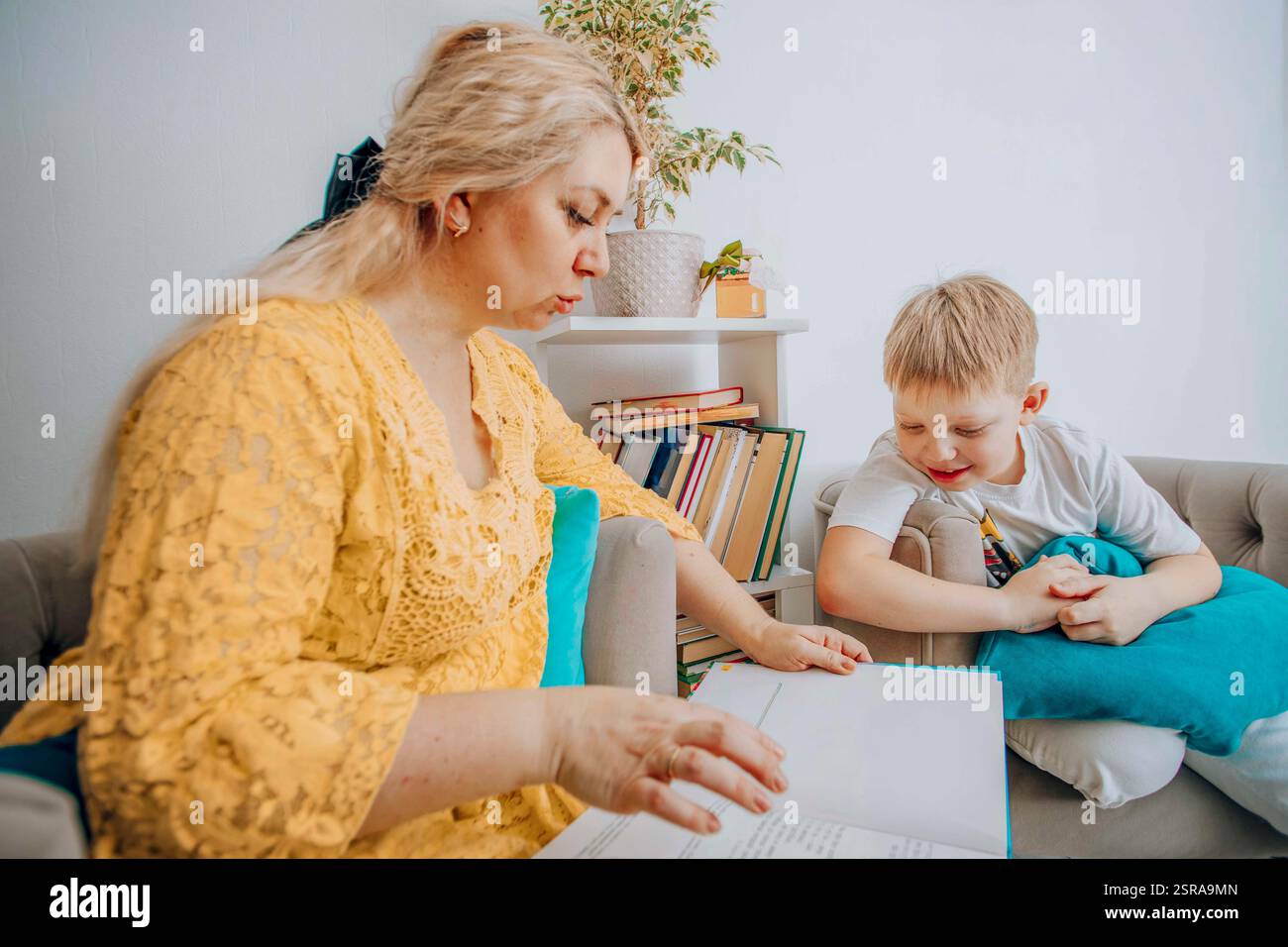 woman in yellow dress reading a book to a smiling boy with blue pillow ...