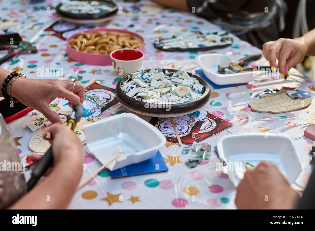 Hands piece together mosaic art with ceramic tiles. Colorful table ...