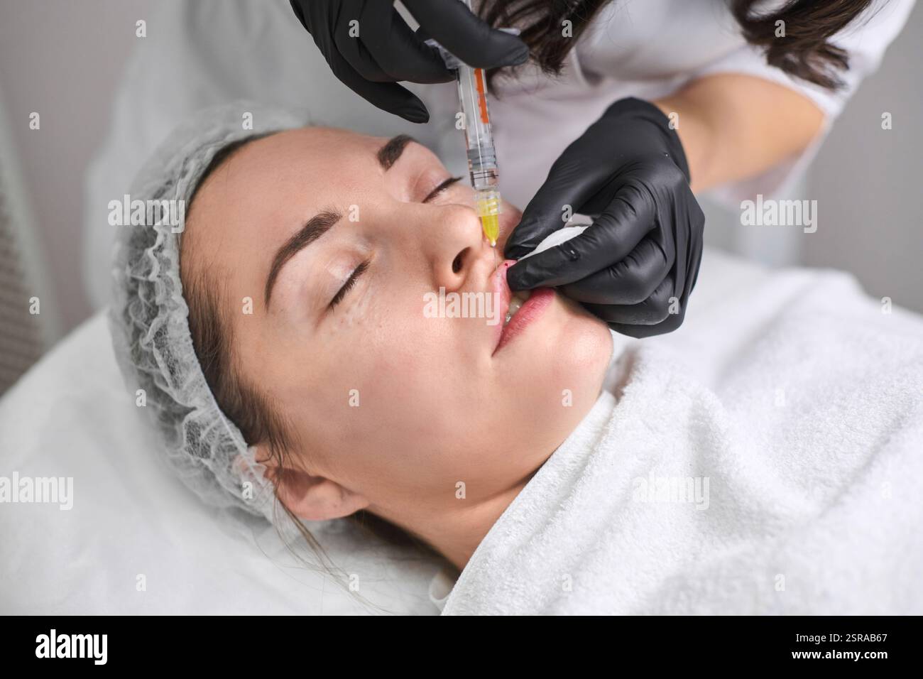 Professional administers dermal filler injection to relaxed young woman ...