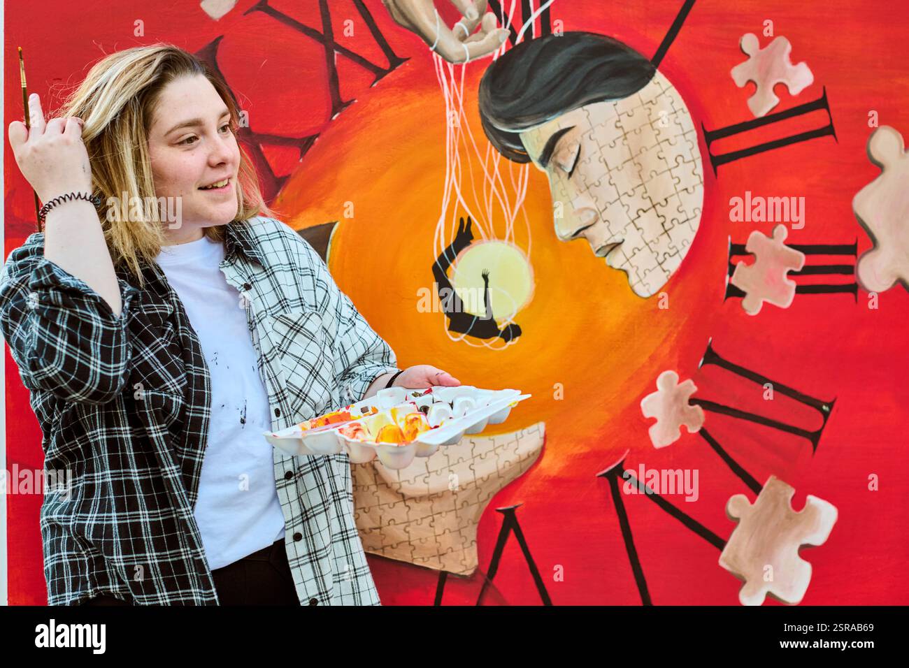 Young female artist with blonde hair paints vivid outdoor mural. Bright ...