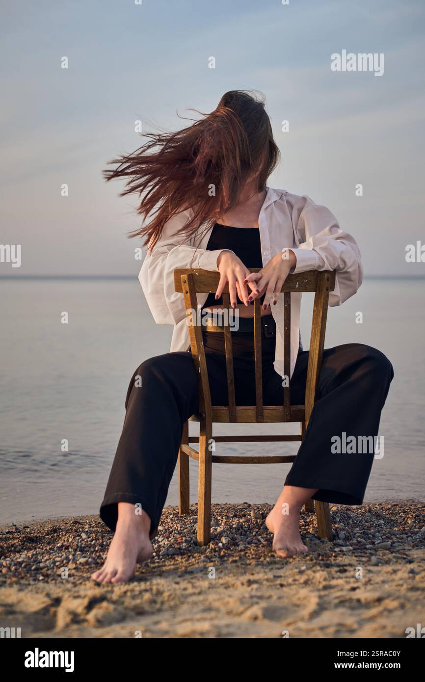 Young woman sits on chair facing calm sea, symbolizing solitude and ...