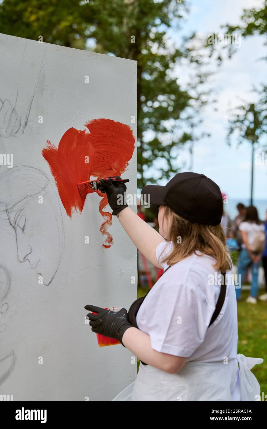 Young female artist in black cap painting with red brush strokes on ...
