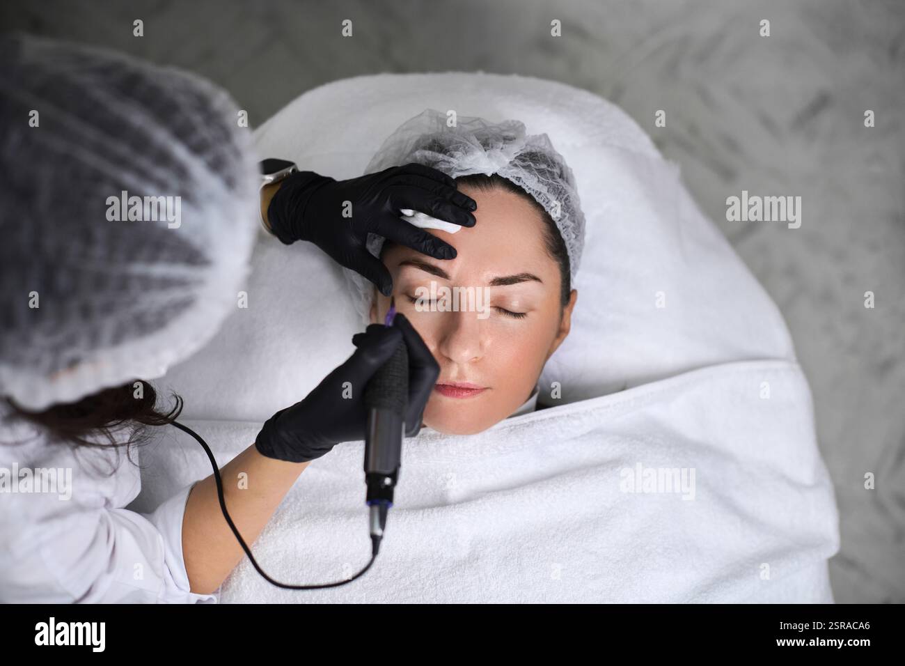 Professional performs eyebrow permanent makeup procedure on relaxed ...