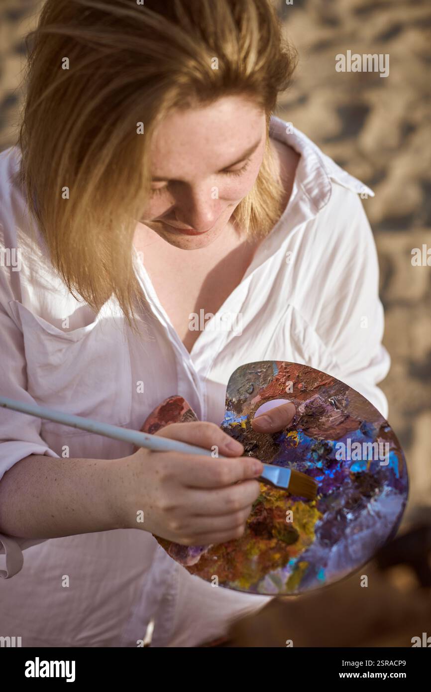 Young female artist paints with vibrant colors on palette in natural ...