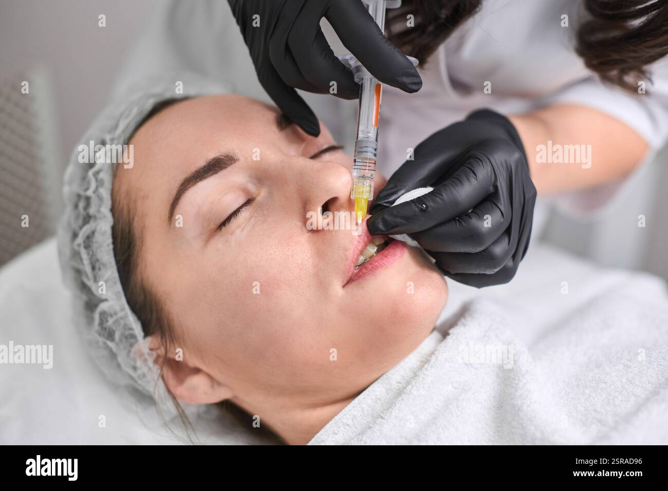 Professional administers dermal filler injection to relaxed young woman ...