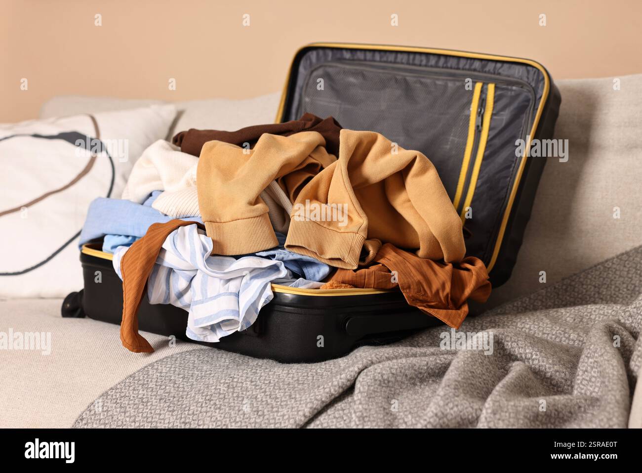 Open suitcase full of different messy clothes on sofa indoors Stock ...