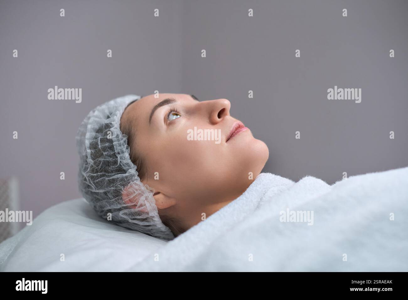 Young woman lies calmly in medical environment, wearing hair cap and ...